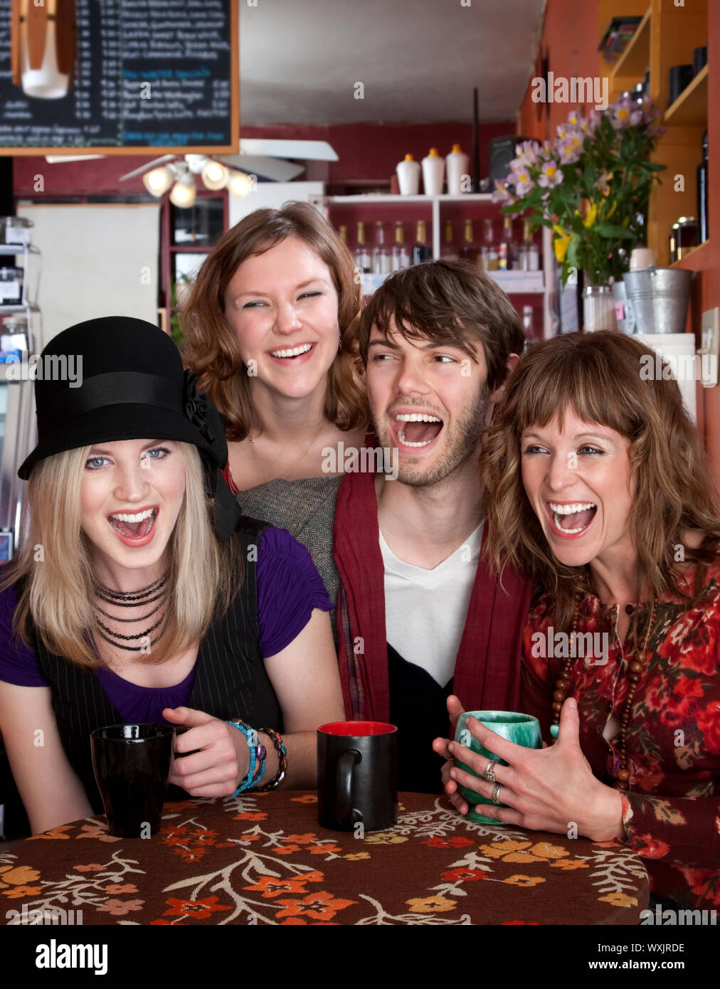 Four young friends laughing in a cafe Stock Photo - Alamy
