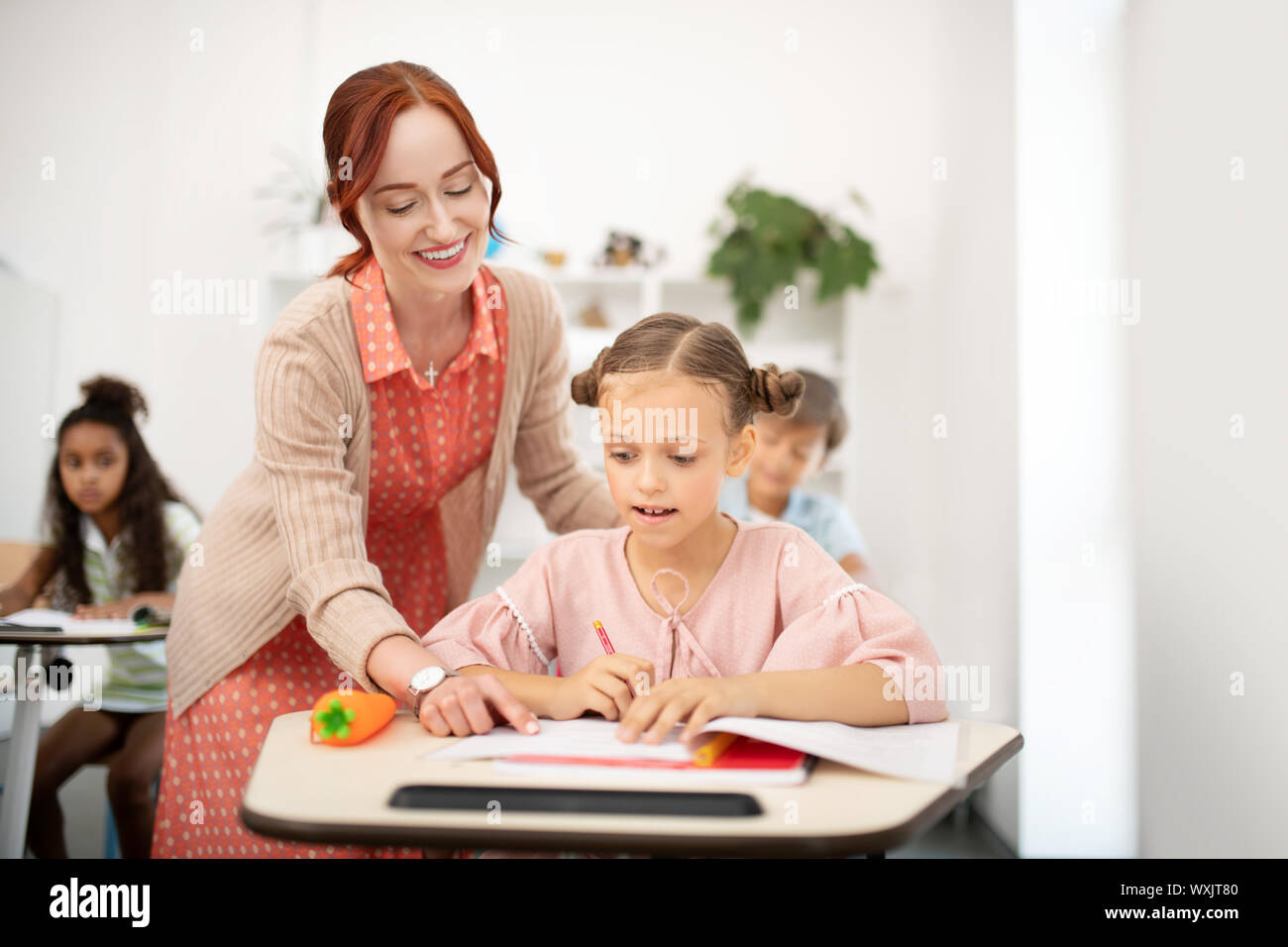 Smiling teacher helping girl with writing down letters Stock Photo - Alamy