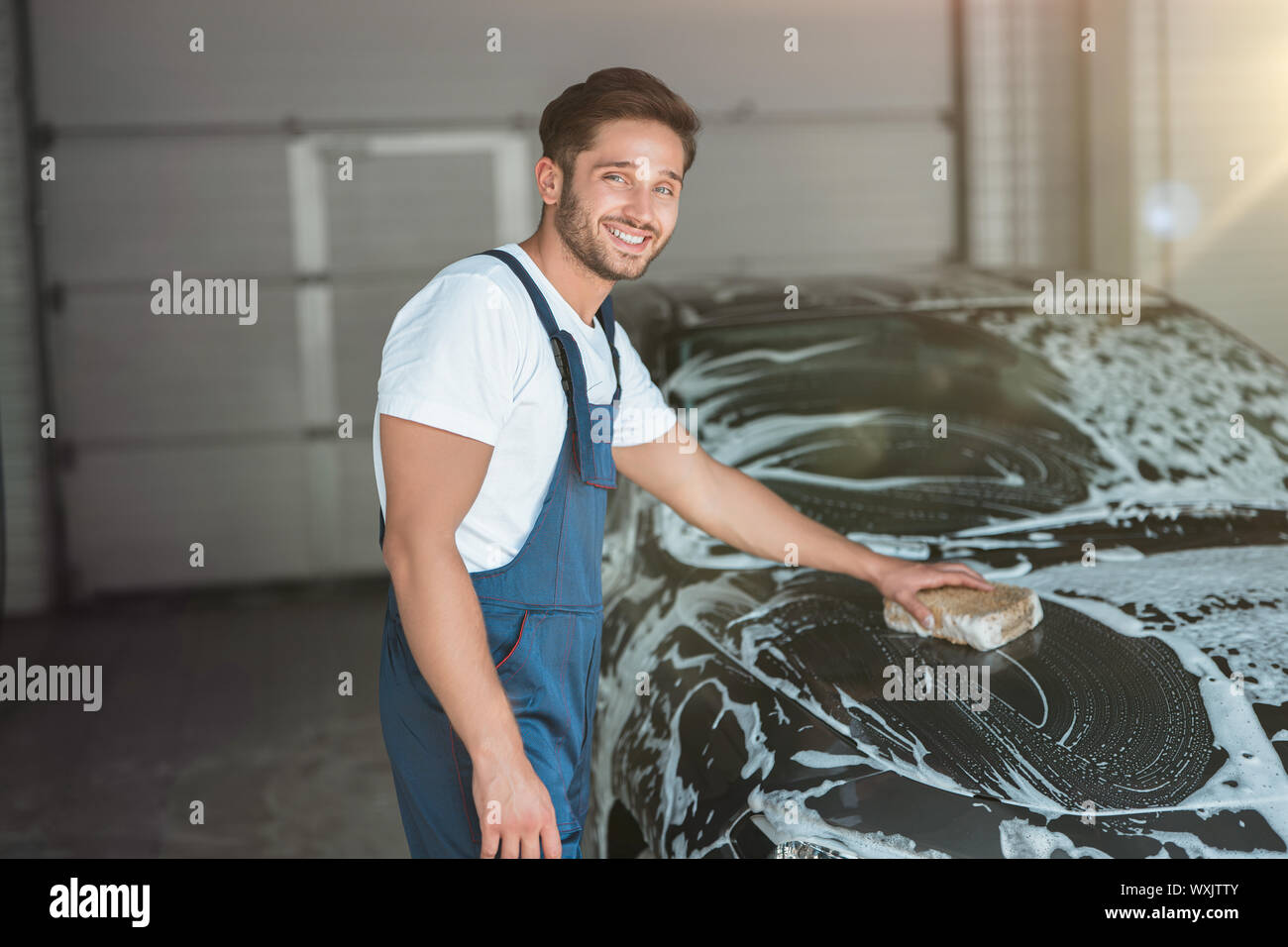 young handsome man wearing uniform washing car with sponge at car ...