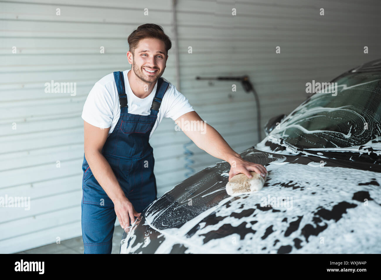 young handsome smiling man wearing uniform washing car with sponge at ...