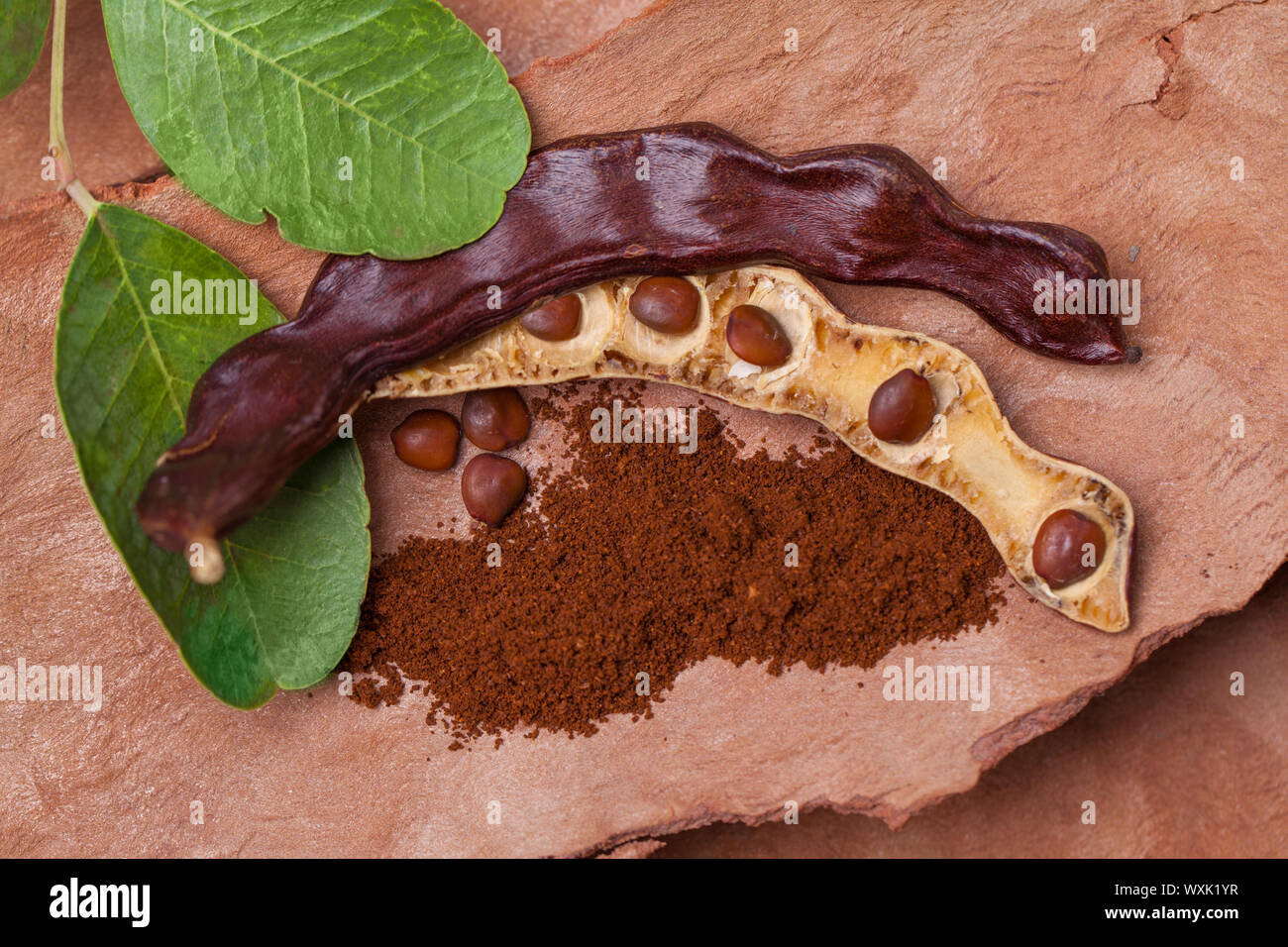 Carob. Organic carob pods with seeds and leaves on tree bark table ...