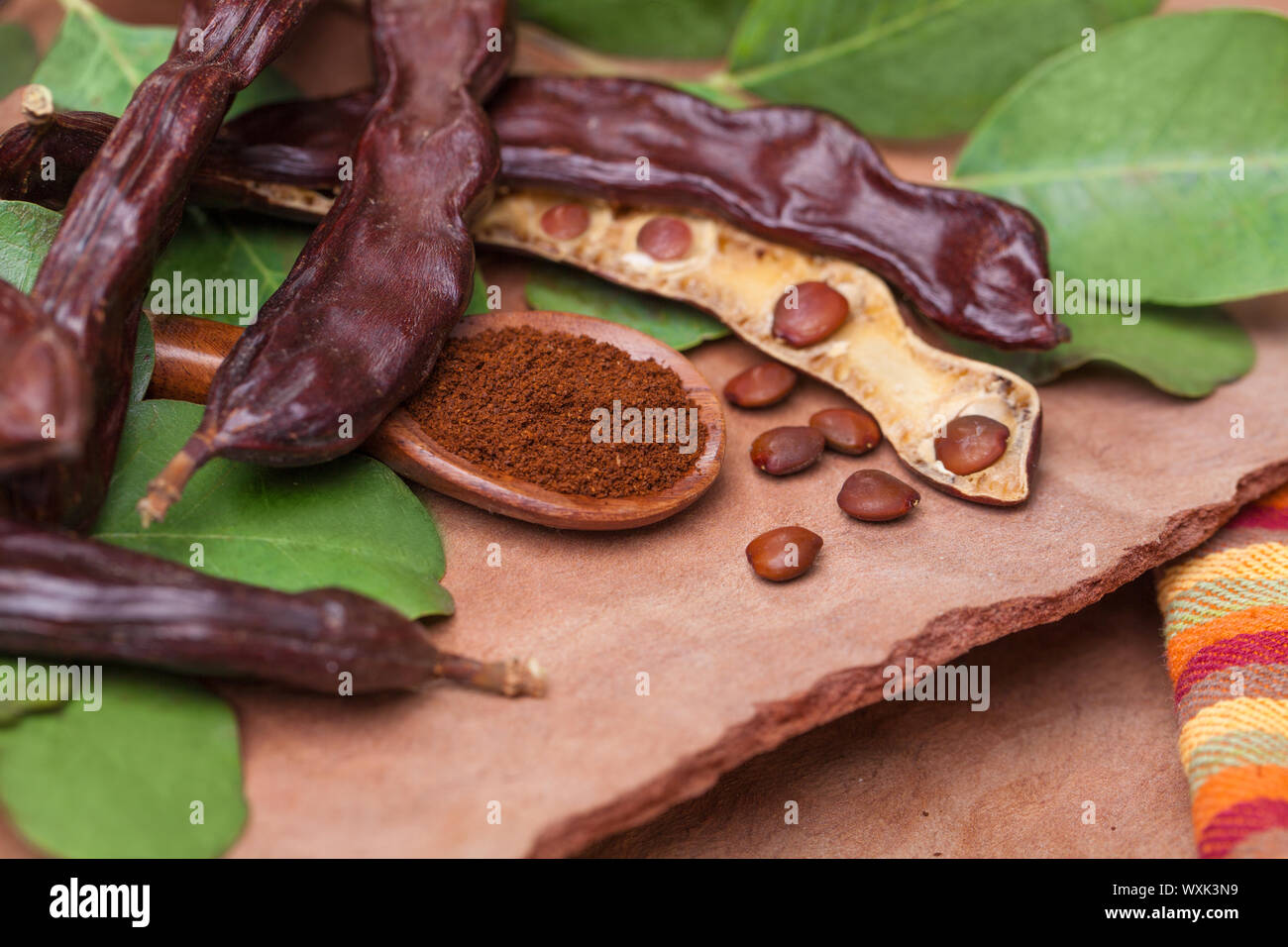 Carob. Organic carob pods with seeds and leaves on tree bark table ...