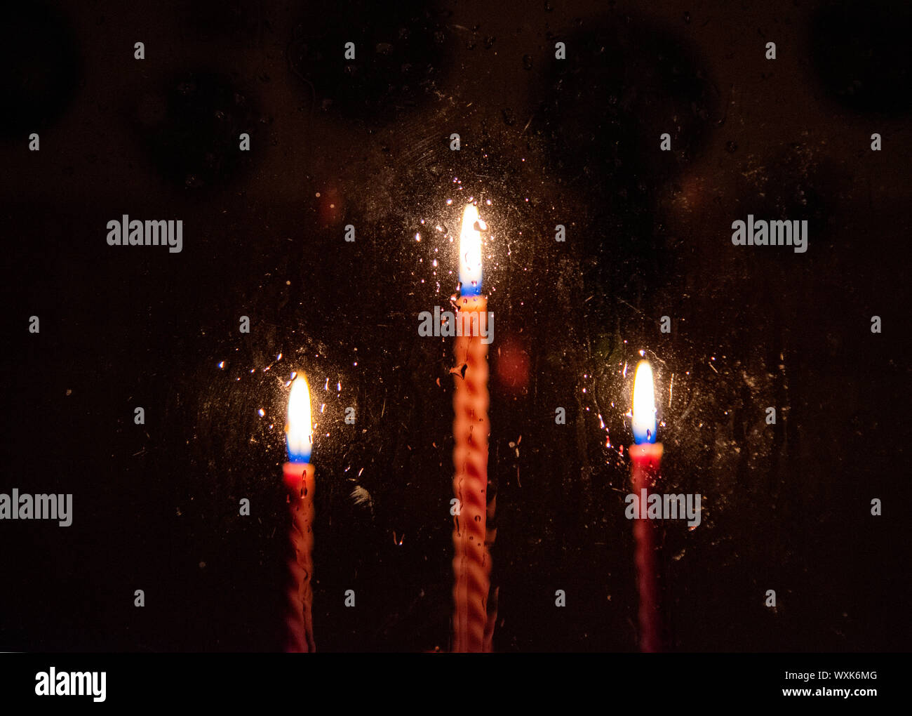 Three blurred red candles burning in the darkness outside the window ...