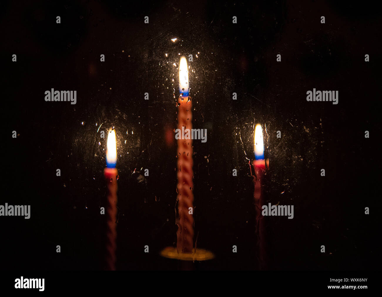 Three blurred red candles burning in the darkness outside the window ...