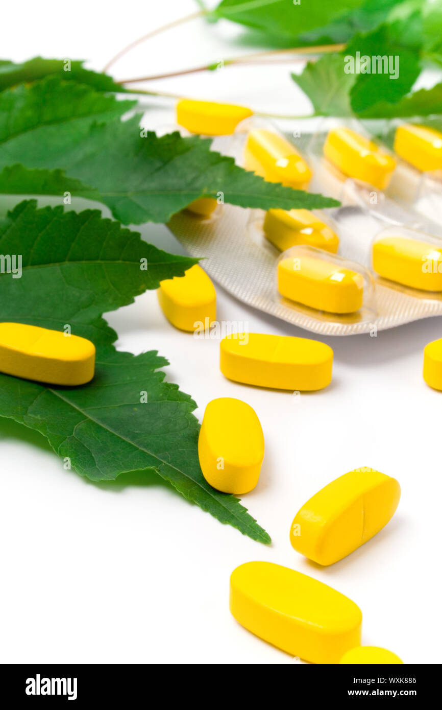 yellow vitamin pills and green leaves on white background Stock Photo ...