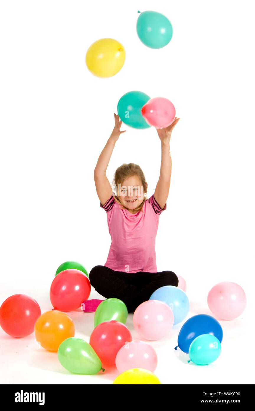 A blond girl throwing balloons in the air while sitting on the ground ...