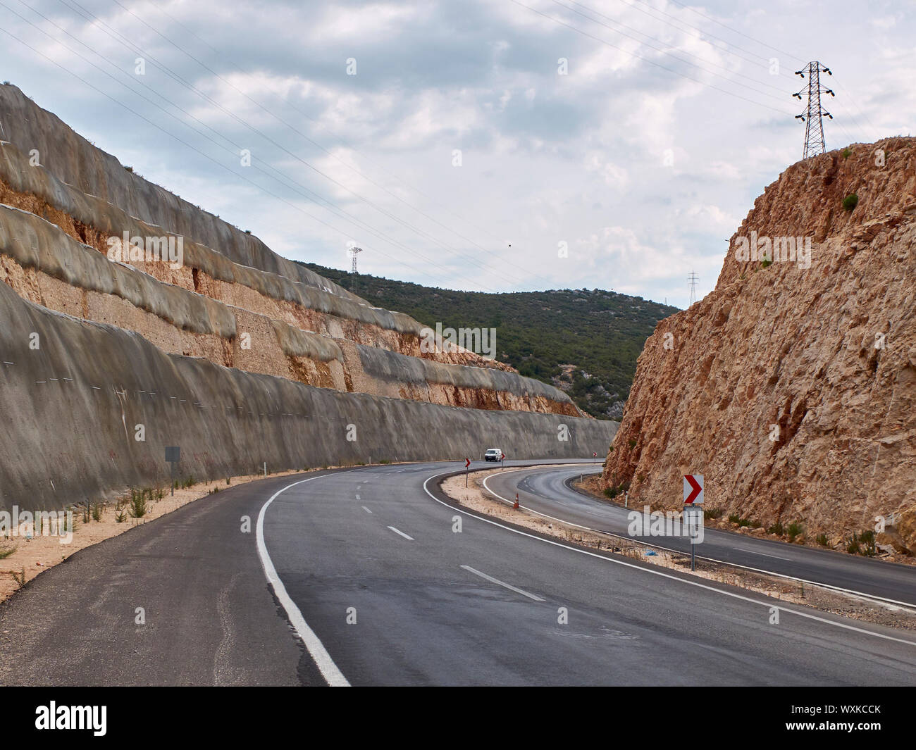 Asphalt road curves between two rock cliffs with openwork power line ...
