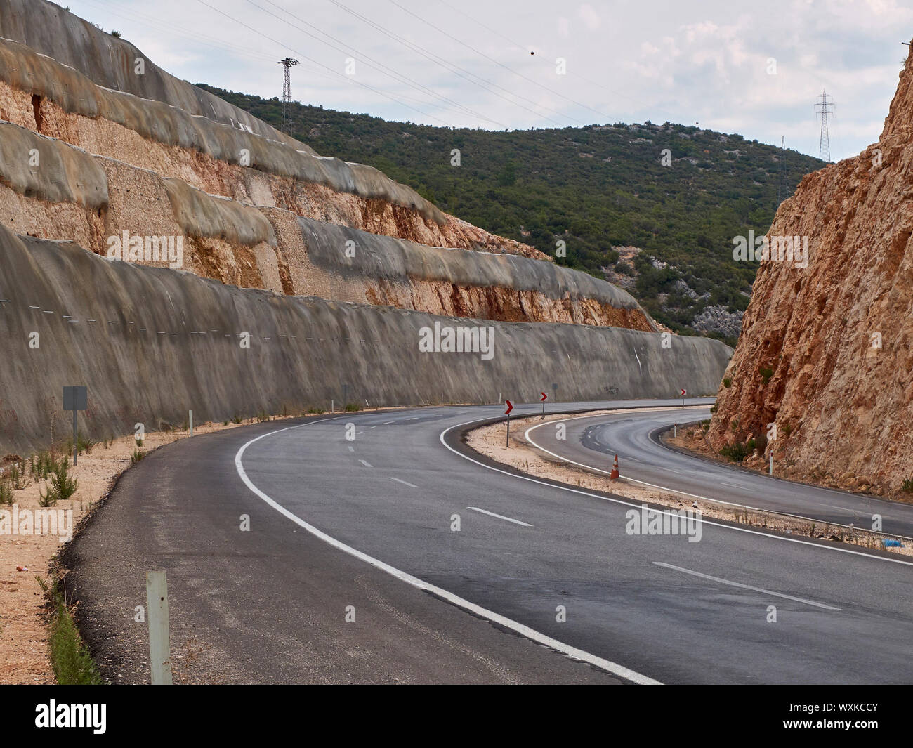 Asphalt road curves between two rock cliffs with openwork power line ...