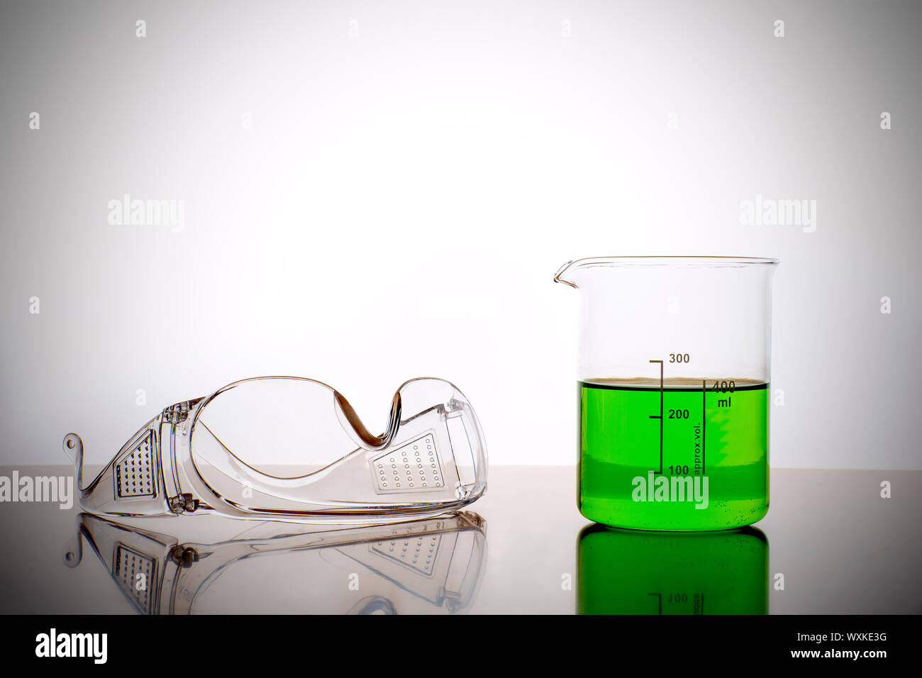 Measuring glass with green liquid and safety glasses, goggles in a ...