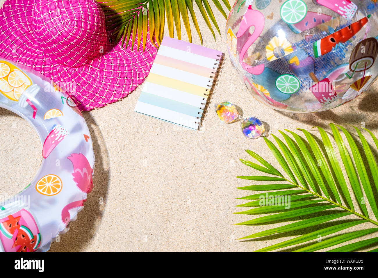 Colourful writing note pad with pink and green pen on sand, surrounded ...