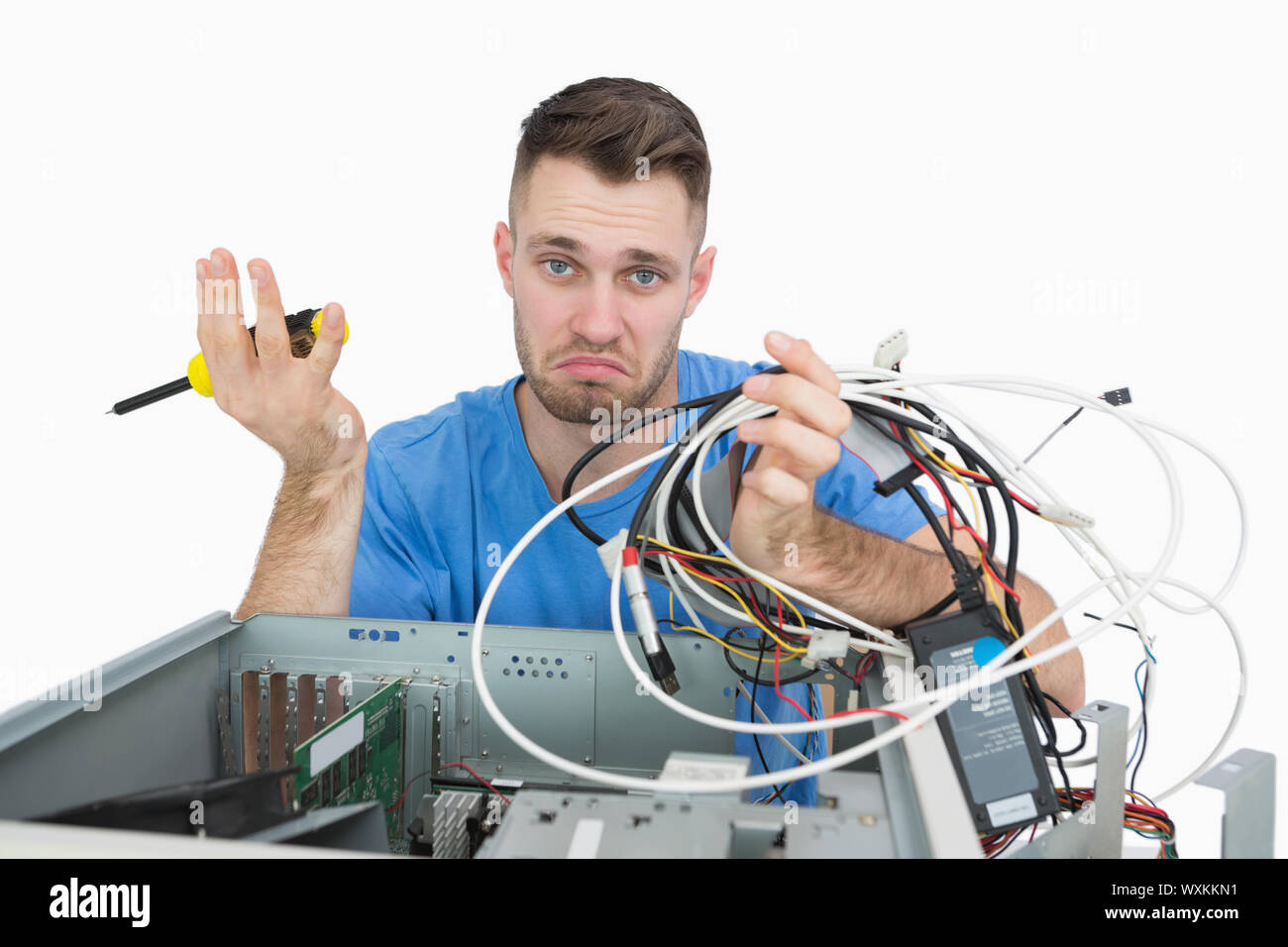 Portrait of confused young it professional with screw driver and cables ...