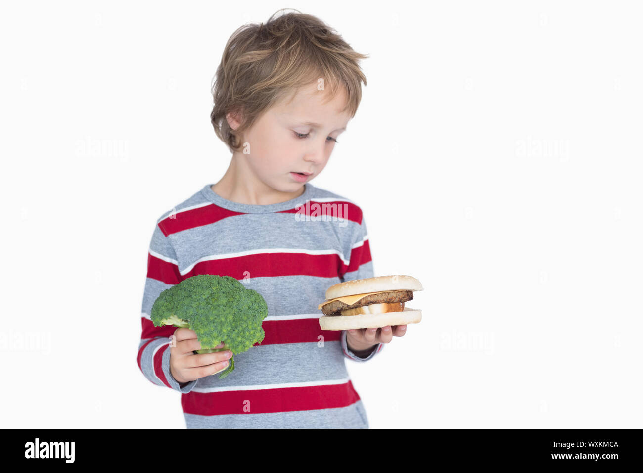 Young boy holding broccoli and burger over white background Stock Photo ...