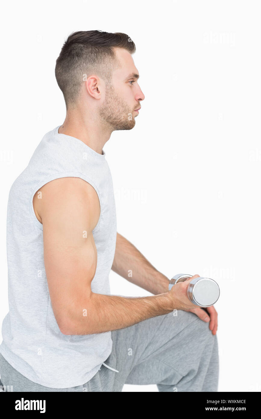 Side view of young man exercising with dumbbell over white background ...
