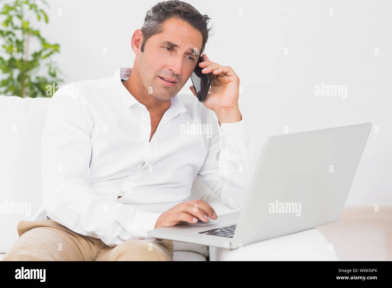Man using the moblie phone and his laptop on couch Stock Photo - Alamy