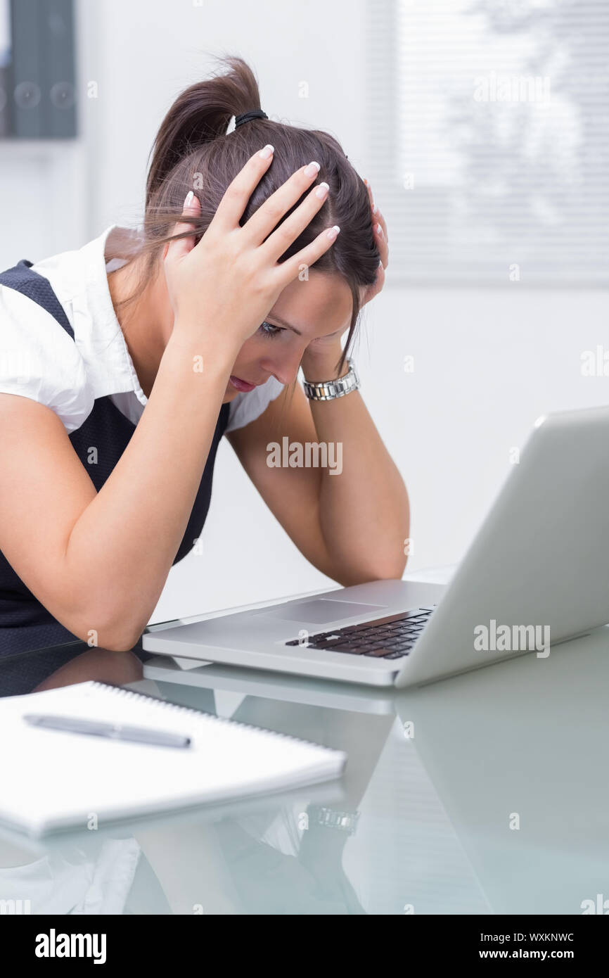 Frustrated business woman sitting with head in hands in front of laptop at office desk Stock ...