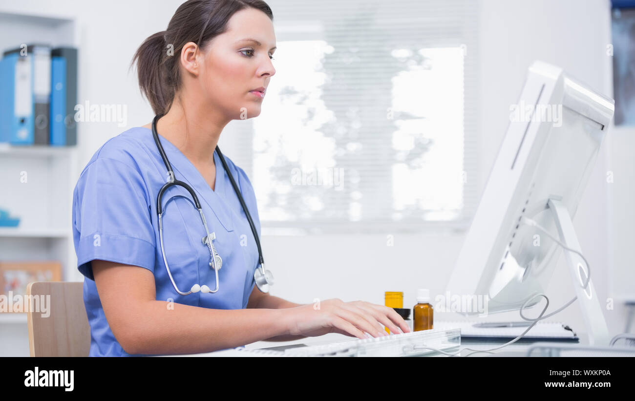 Side view of young female surgeon using computer at desk in clinic ...
