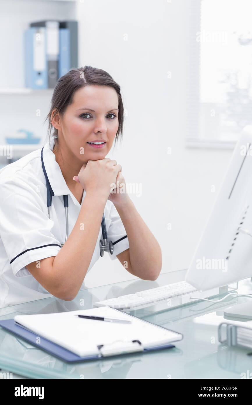 Portrait of young female nurse with hands under chin in front of ...