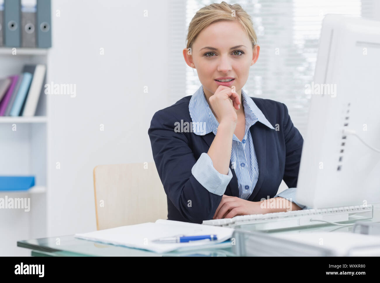 Portrait of young confident business woman with computer at office desk ...
