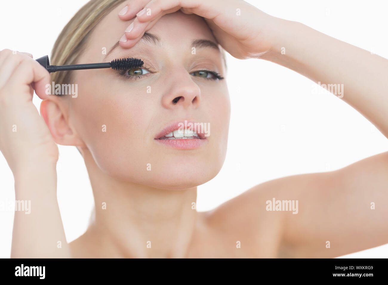 Closeup portrait of young woman applying mascara to her eye over white ...