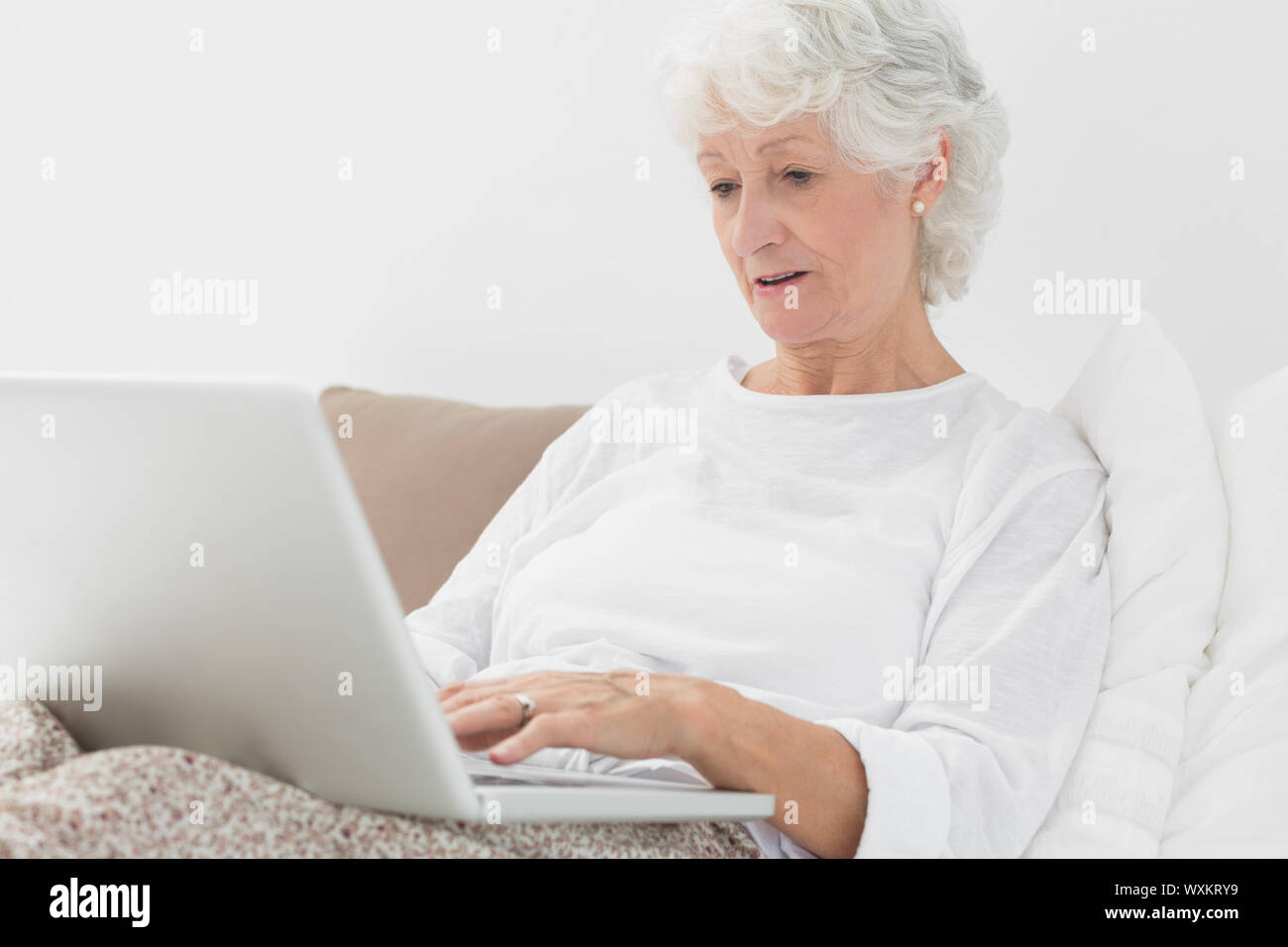 Old woman typing on her laptop lying on her bed Stock Photo - Alamy
