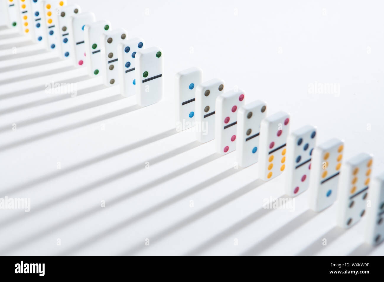 Line of colourful dominoes with one piece missing on white surface ...