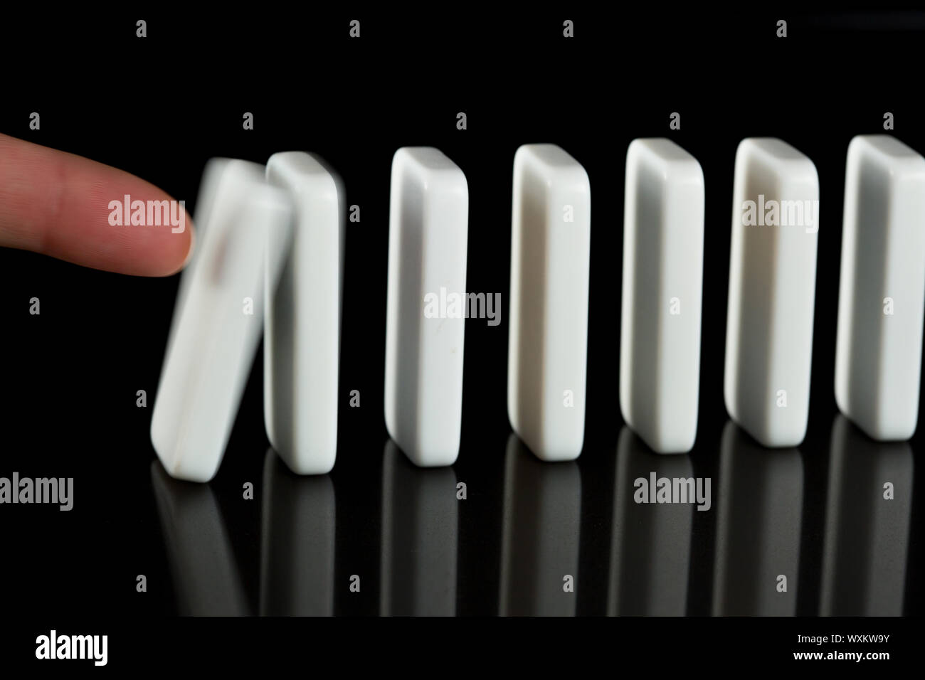 Finger pushing over dominoes on black background Stock Photo - Alamy