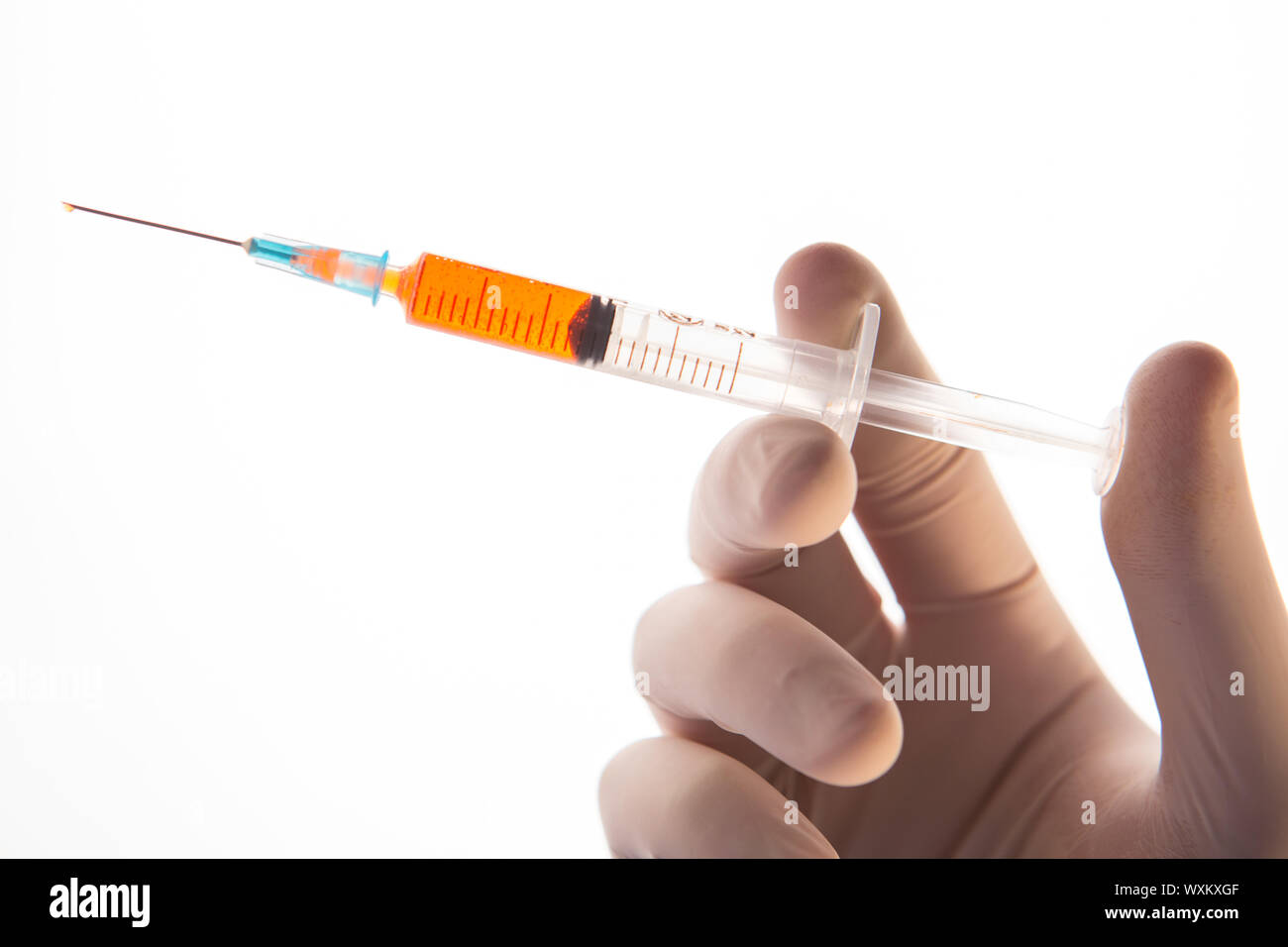 Gloved hand holding hypodermic needle with orange liquid on white ...