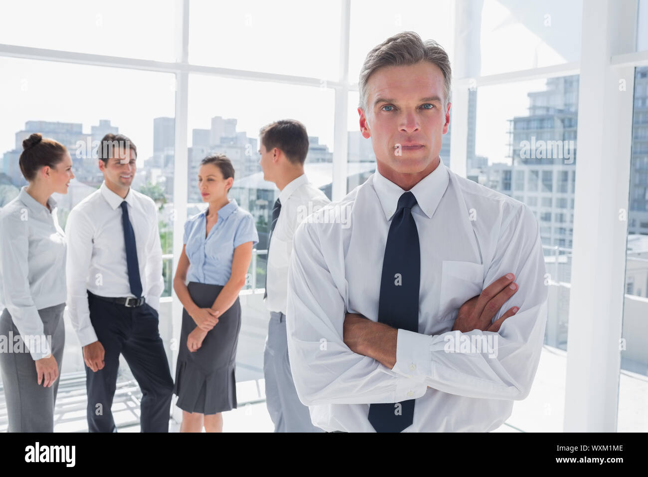 Boss with arms folded standing in a modern office with colleagues ...