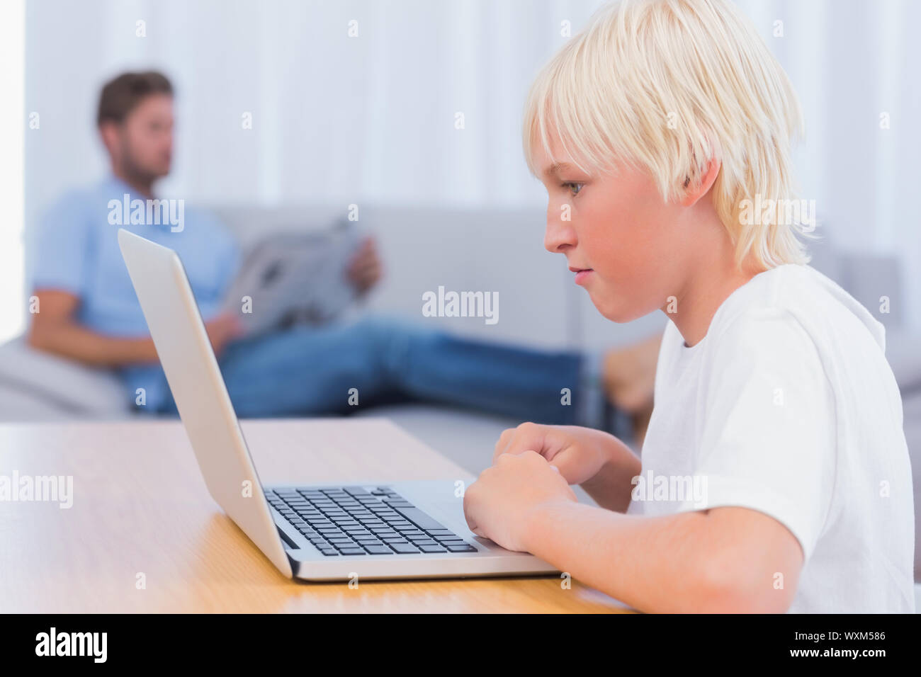 Boy using laptop while his father is reading on the couch in the living ...