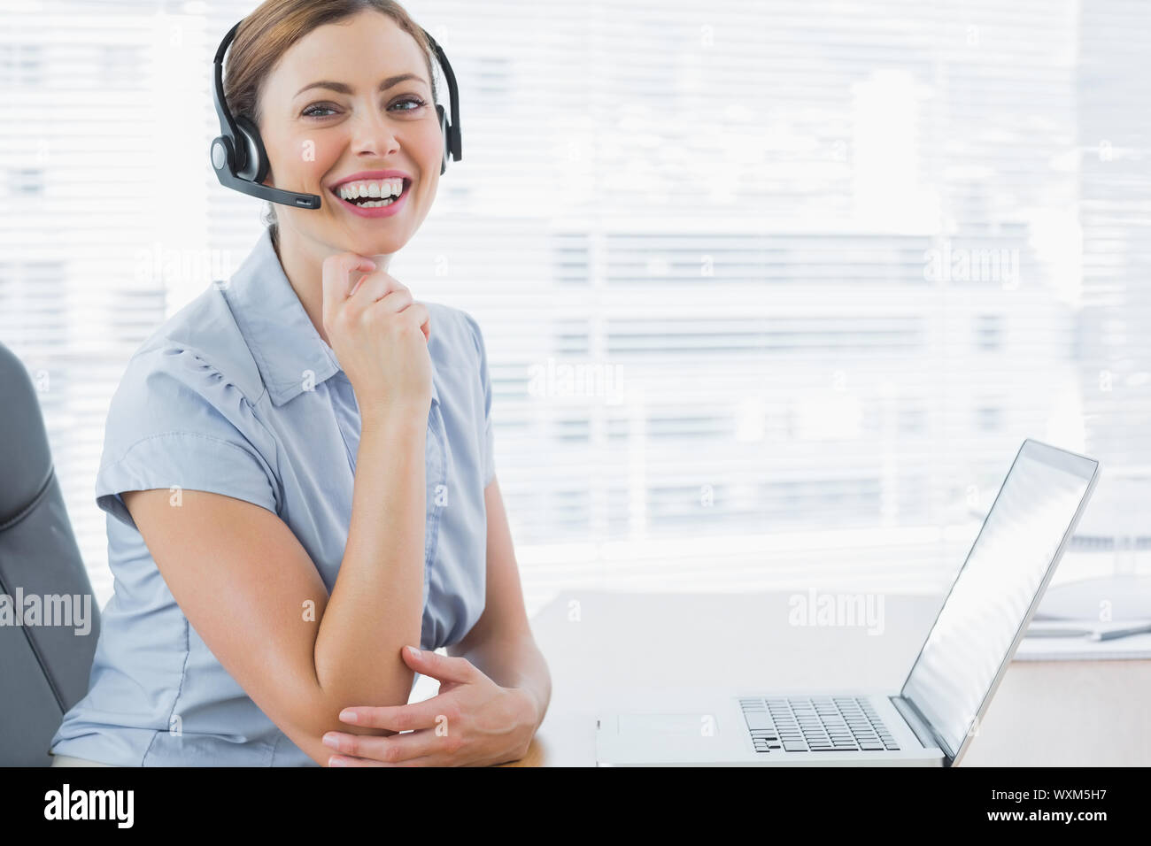 Laughing call centre agent wearing headset at her desk with laptop in ...