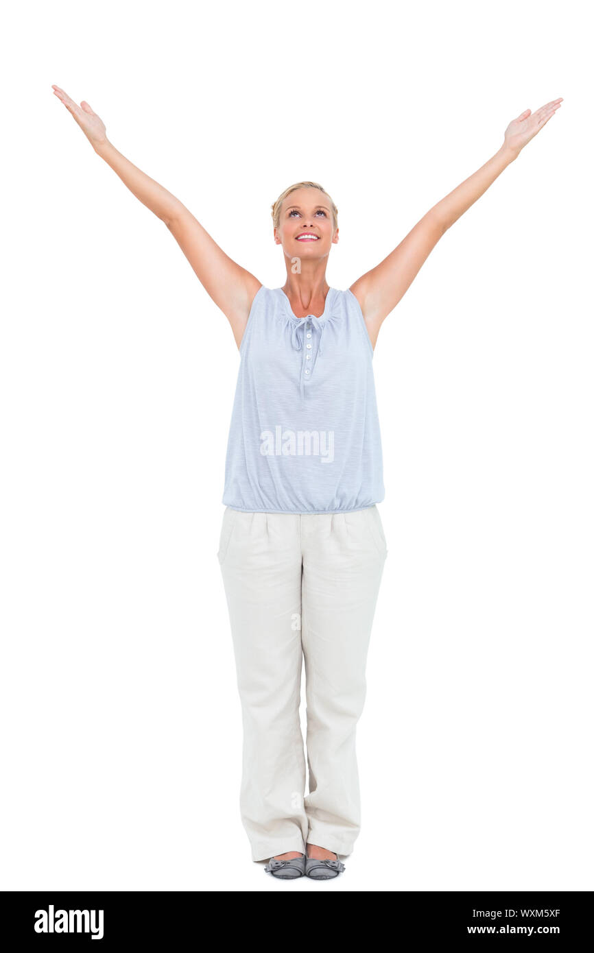 Happy blonde woman standing with hands up in air on white background ...