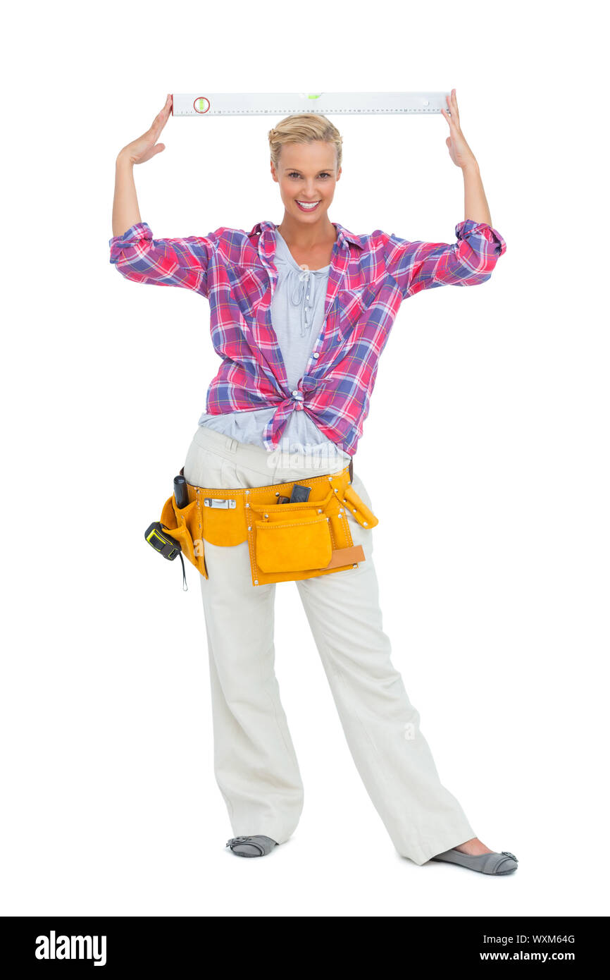 Blonde woman standing while putting a spirit level on her head on white ...