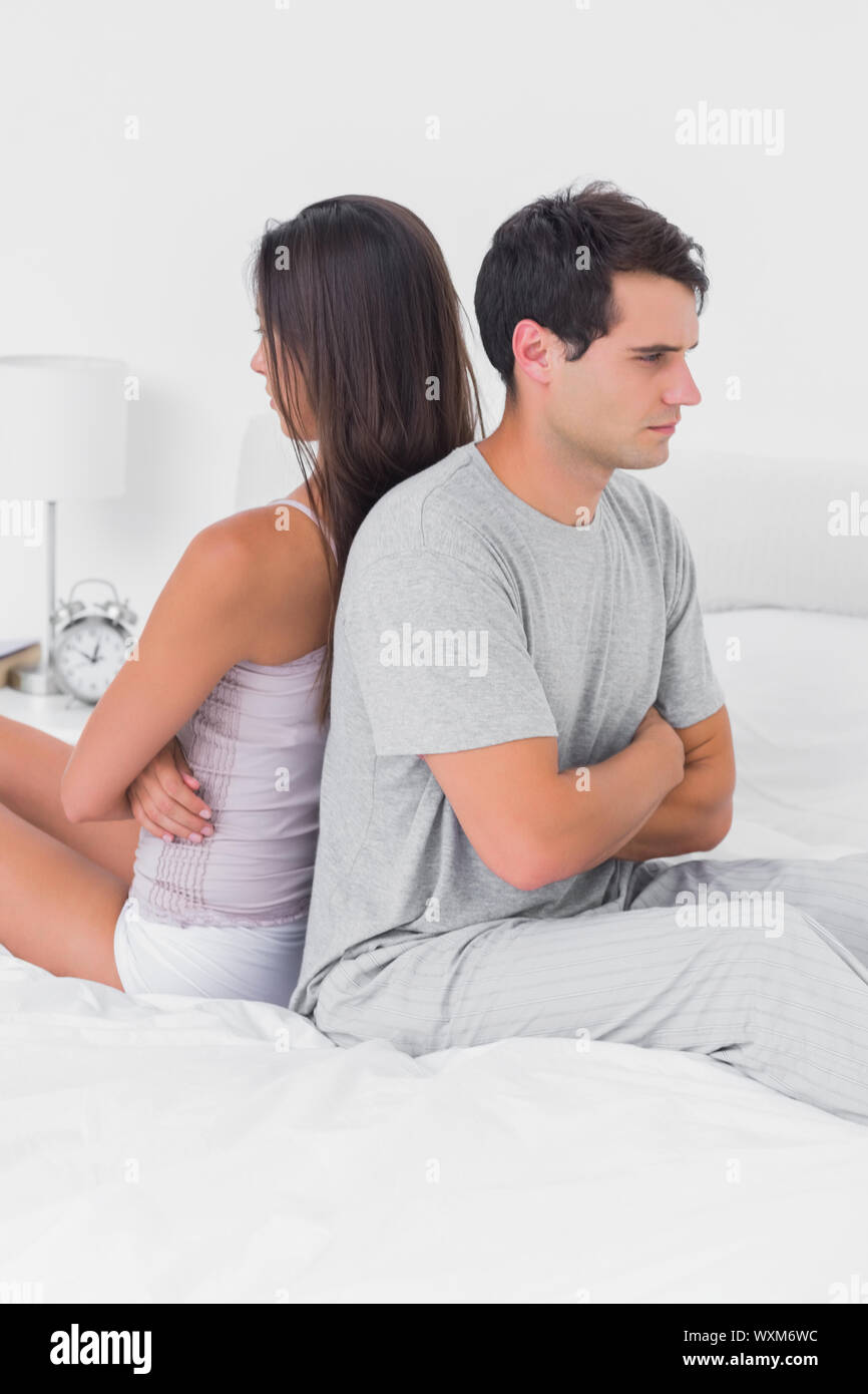 Angry couple ignoring each other sitting back to back on bed during a ...