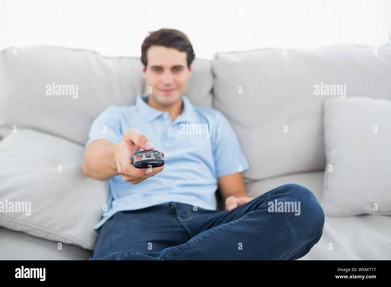 Man changing channel sitting on a couch Stock Photo - Alamy