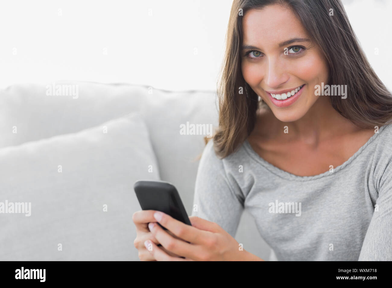 Portrait of a woman texting while she is sat on a couch Stock Photo - Alamy