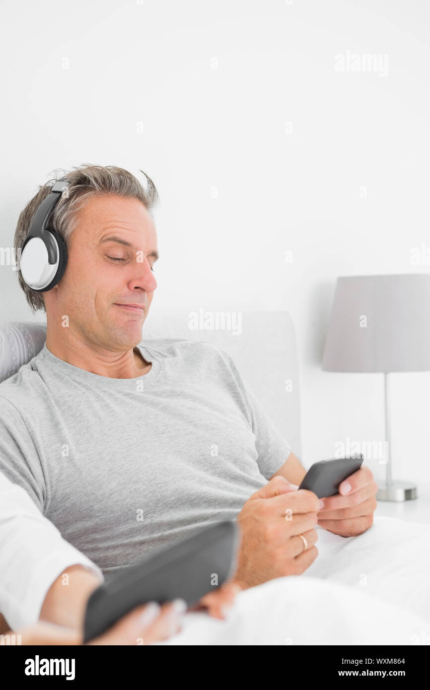 Smiling Man Listening To Music On His Smartphone At Home In Bed Stock