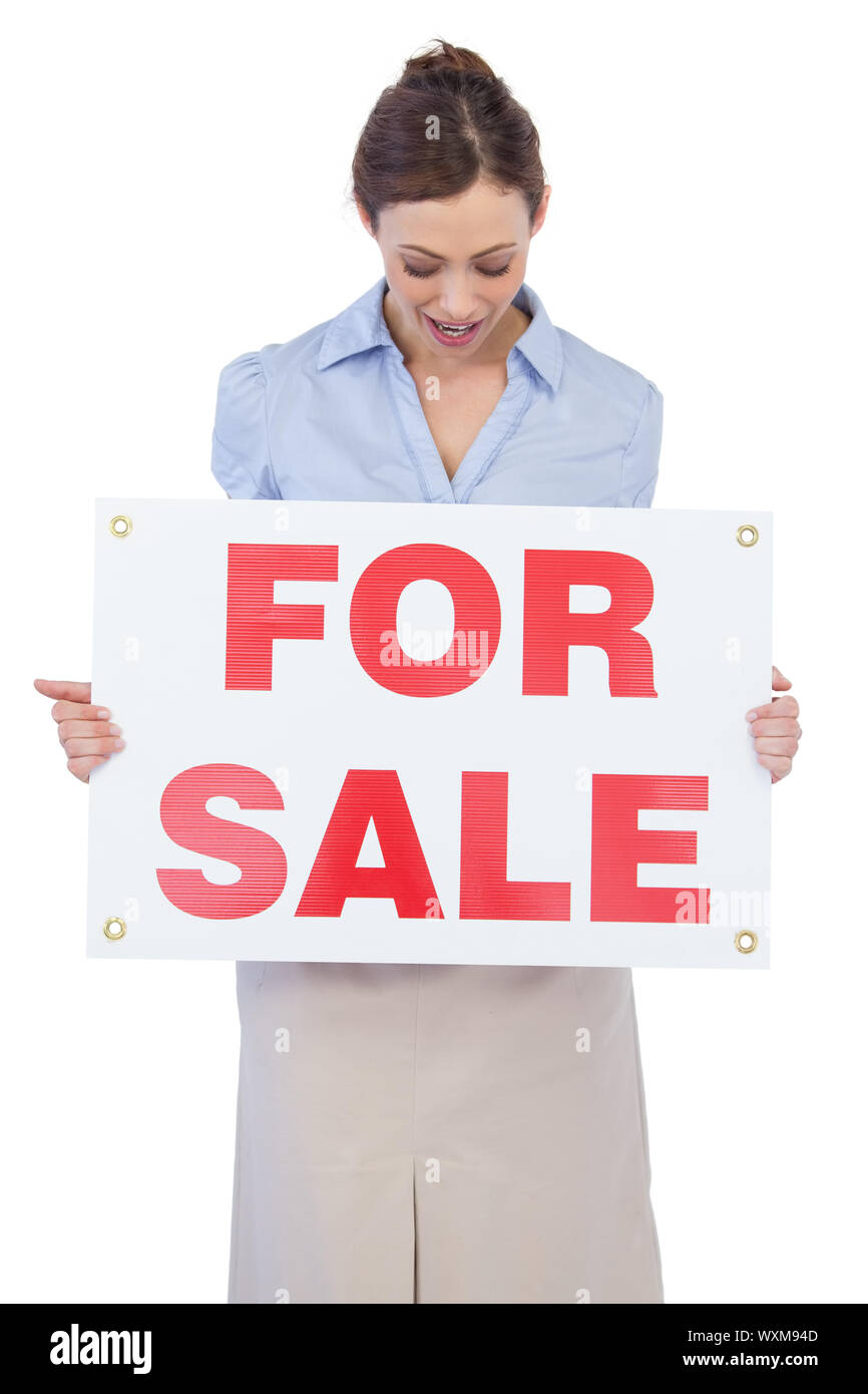 Happy estate agent posing with for sale sign against white background ...