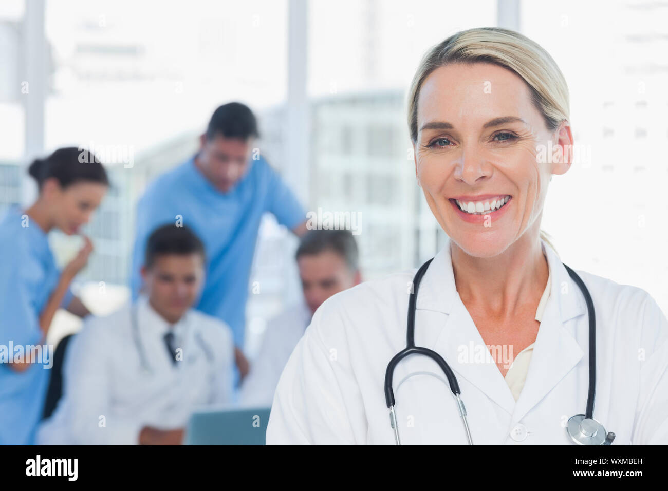 Cheerful blond doctor posing with colleagues in background in medical ...