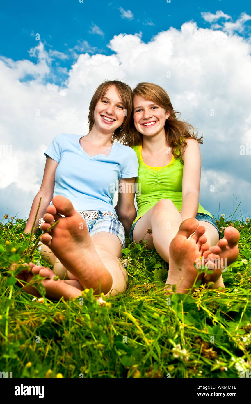 Two young teenage girl friends sitting barefoot on summer meadow Stock ...