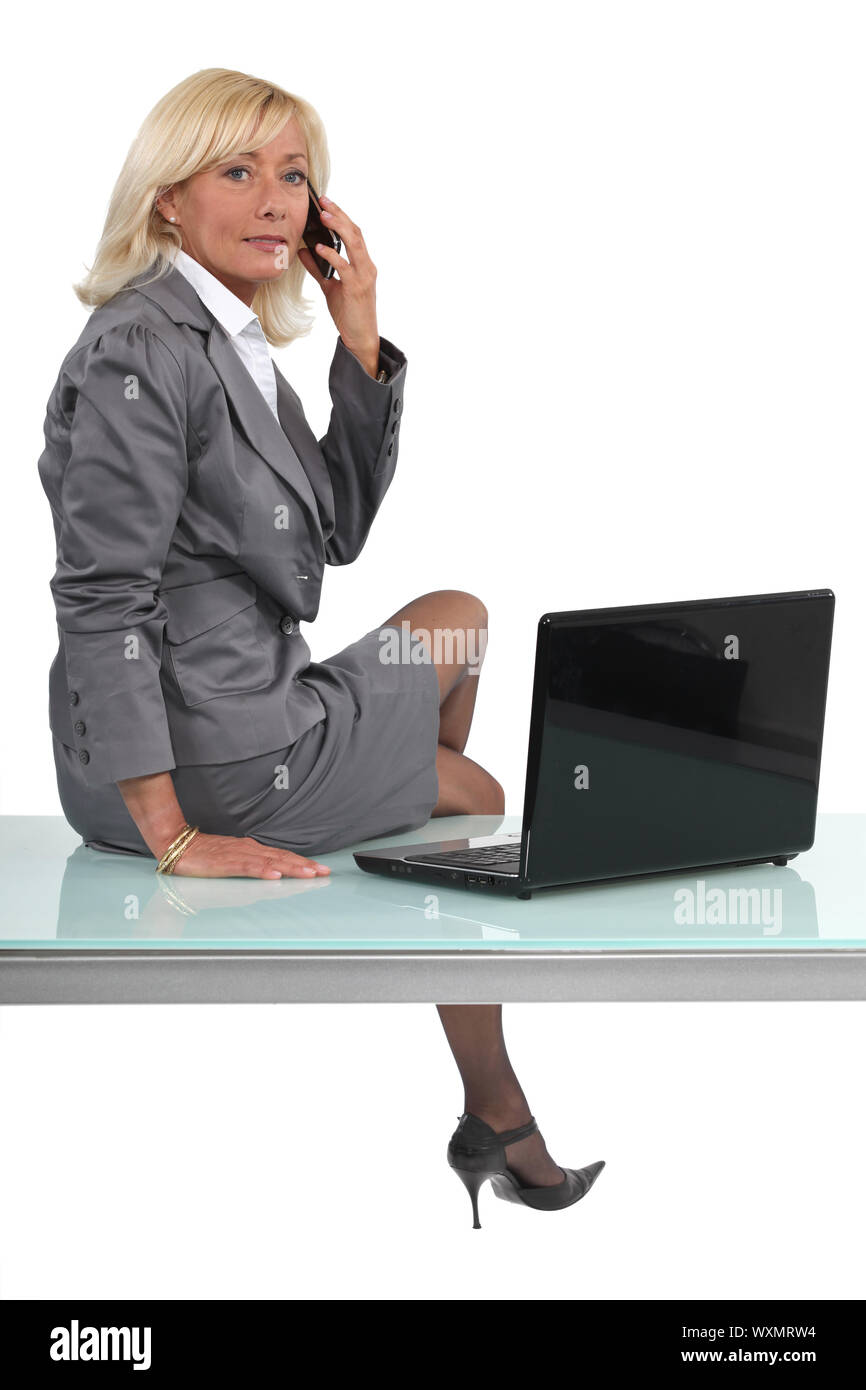 Blond executive sat on desk making call Stock Photo - Alamy