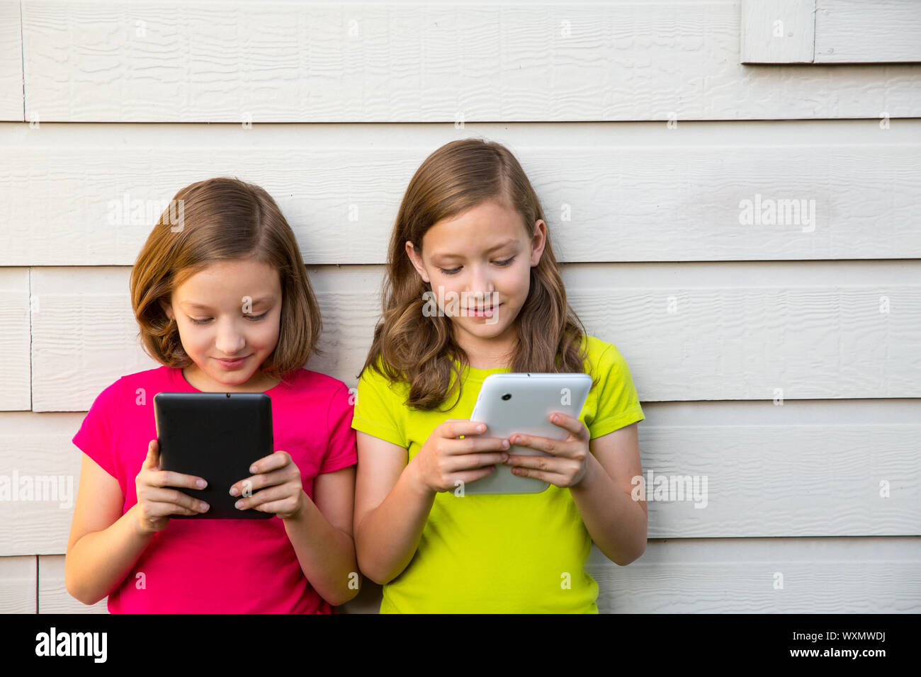 Twin sister girls playing with tablet pc happy on white wall looking ...