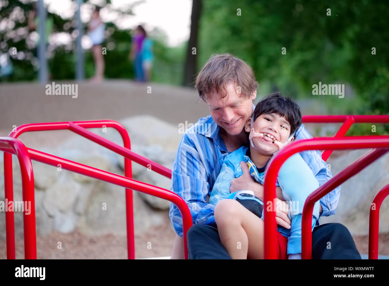 Father playing with disabled son on merry go round at playground. Child ...
