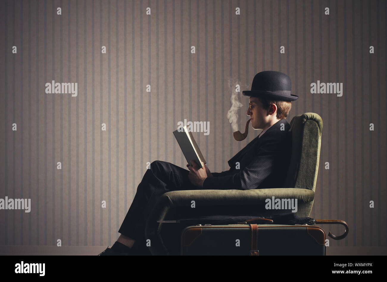 Bizarre man sitting on armchair reading a book and smoking a fake pipe ...