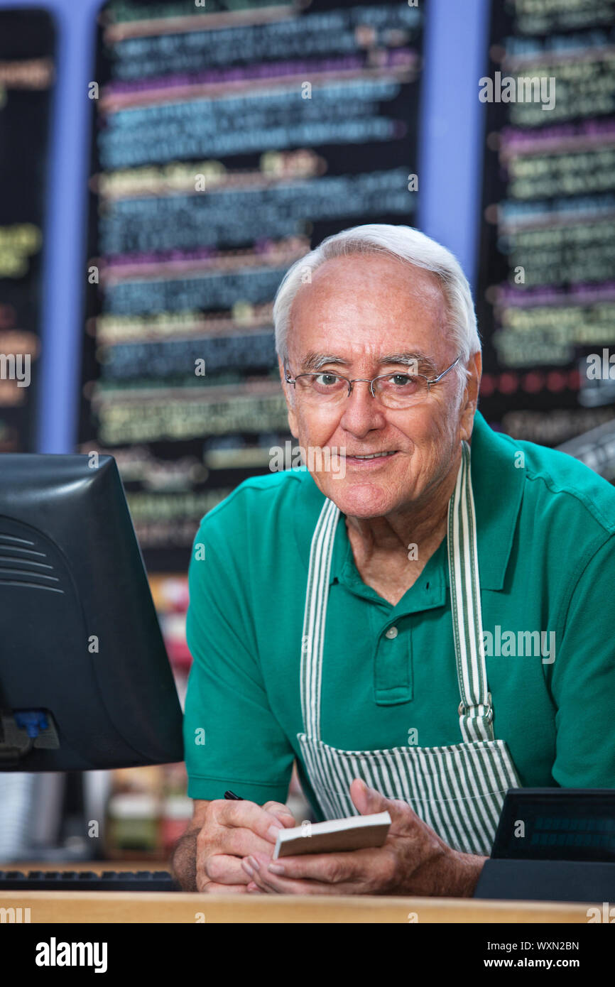 Senior man with apron behind counter taking orders Stock Photo - Alamy