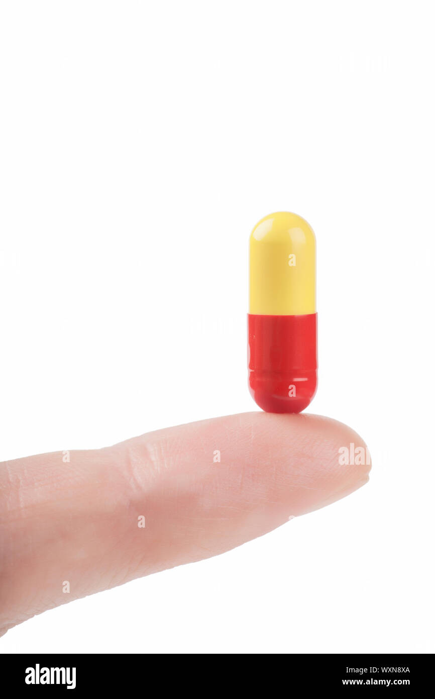 Closeup view of capsule pill on a finger isolated over white background ...