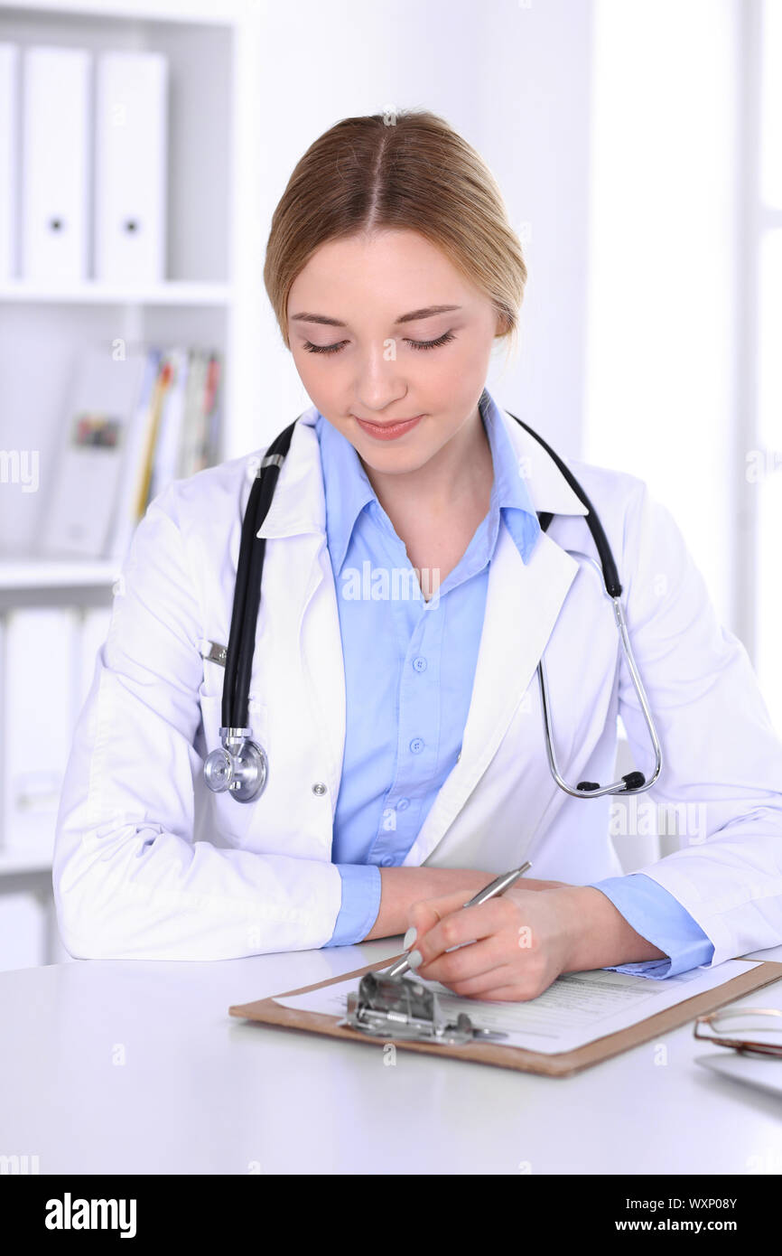Young woman doctor at work while filling up medication history records ...