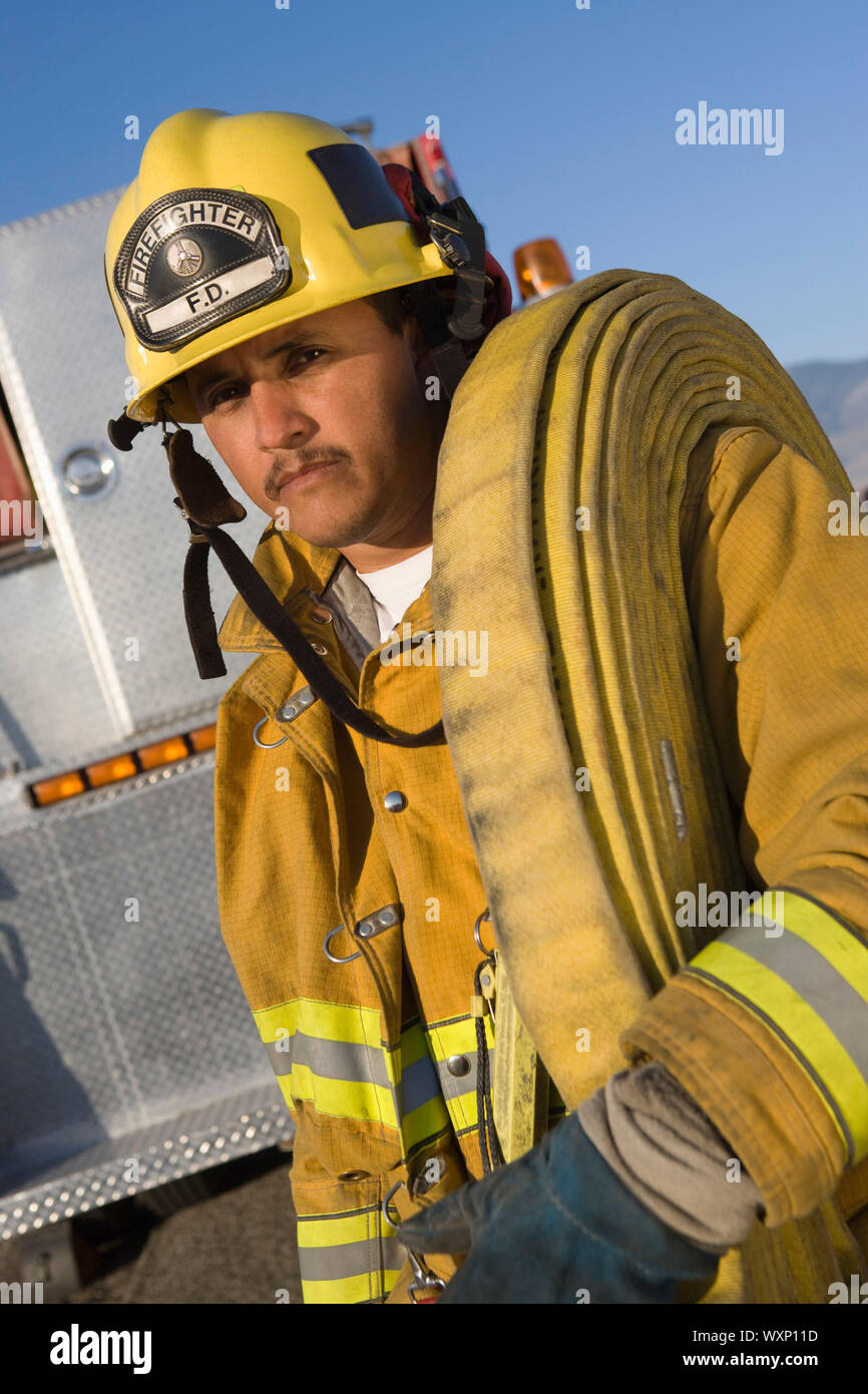 Portrait of firefighter carrying hose Stock Photo - Alamy