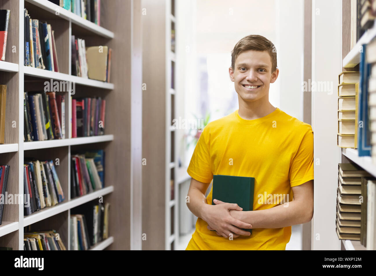 Happy guy student standing between bookshelves in library Stock Photo ...