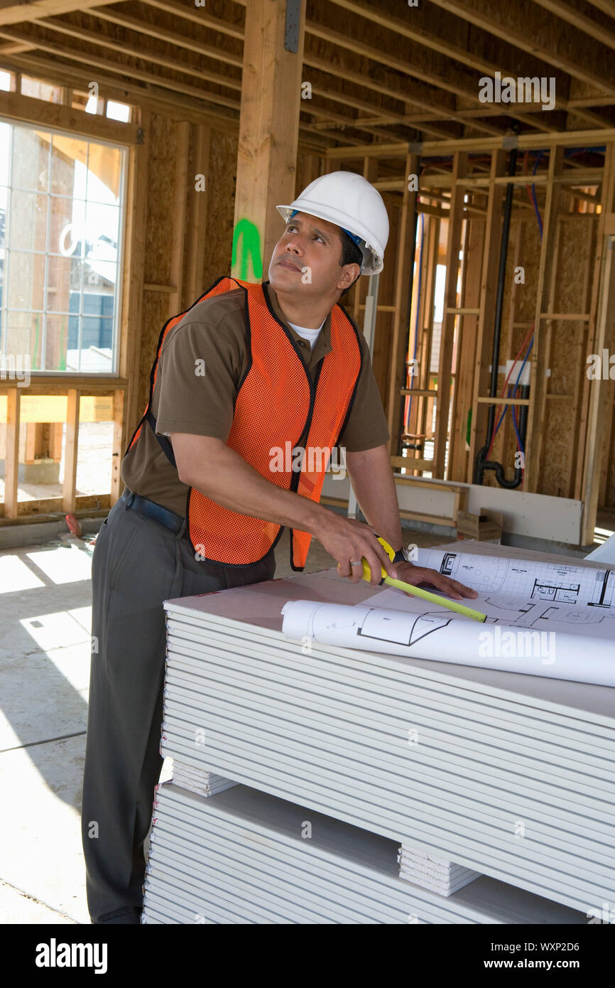 Construction worker using tape measure inside half constructed house ...