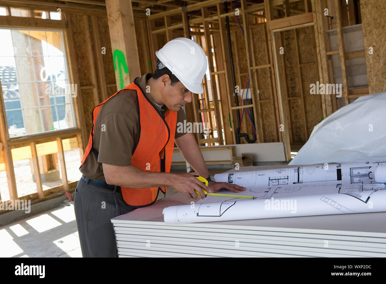 Construction worker using tape measure inside half constructed house ...
